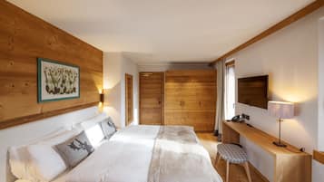 Quarto com cabeceira de madeira, cama com roupa de cama branca, mesa de cabeceira com abajur, escrivaninha com cadeira e um espelho grande na parede.