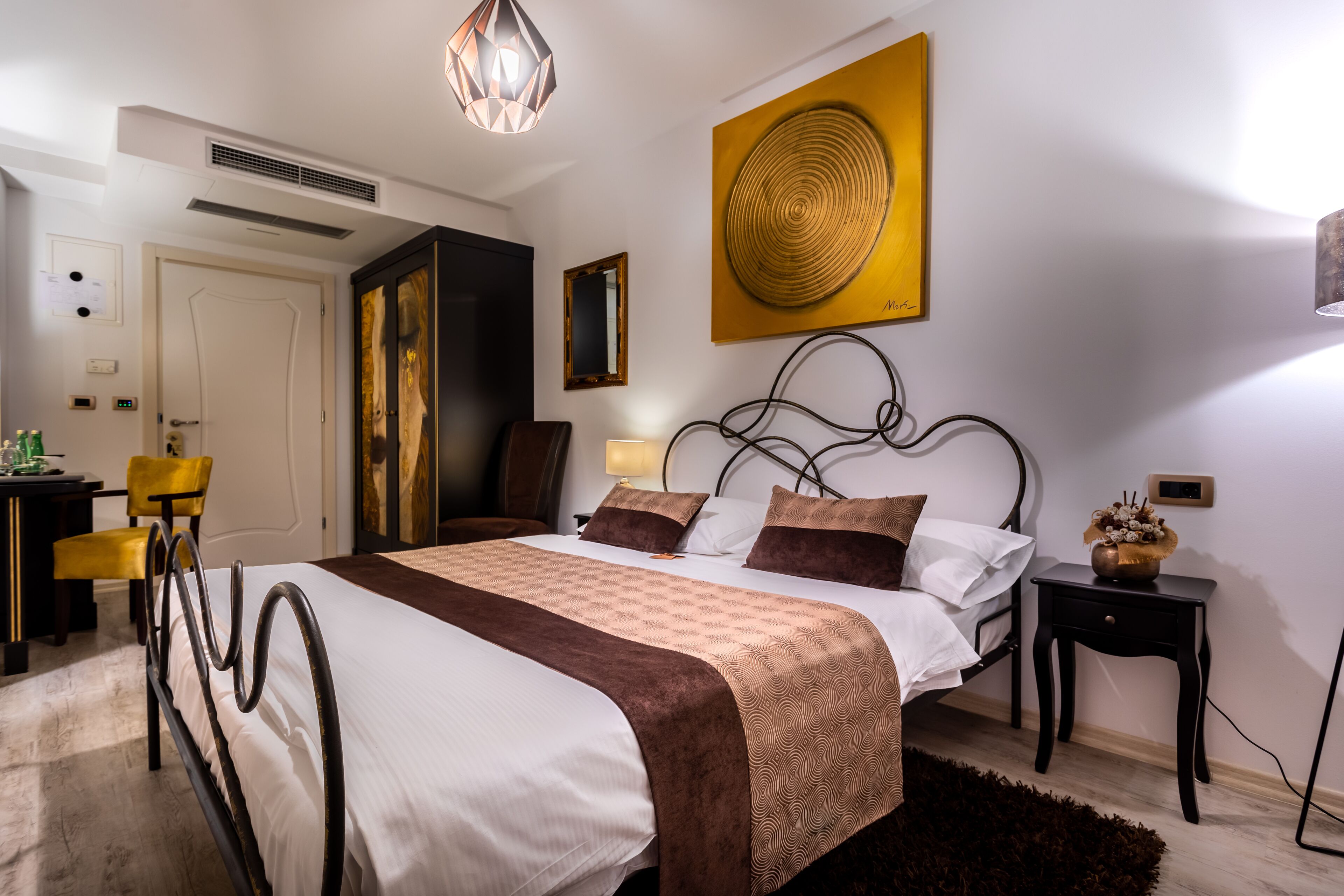 Quarto de hotel com uma cama grande, uma escrivaninha com cadeira, mesa de cabeceira com abajur e uma obra de arte grande na parede.