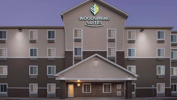 Um hotel com vários andares e uma placa grande com a inscrição 'Woodspring Suites'.