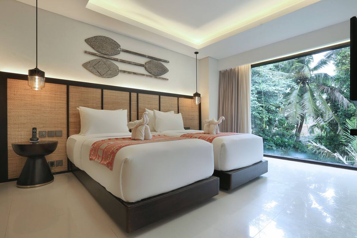 Quarto de hotel moderno com cama grande, mesas de cabeceira, televisão na parede e vista para o verde.