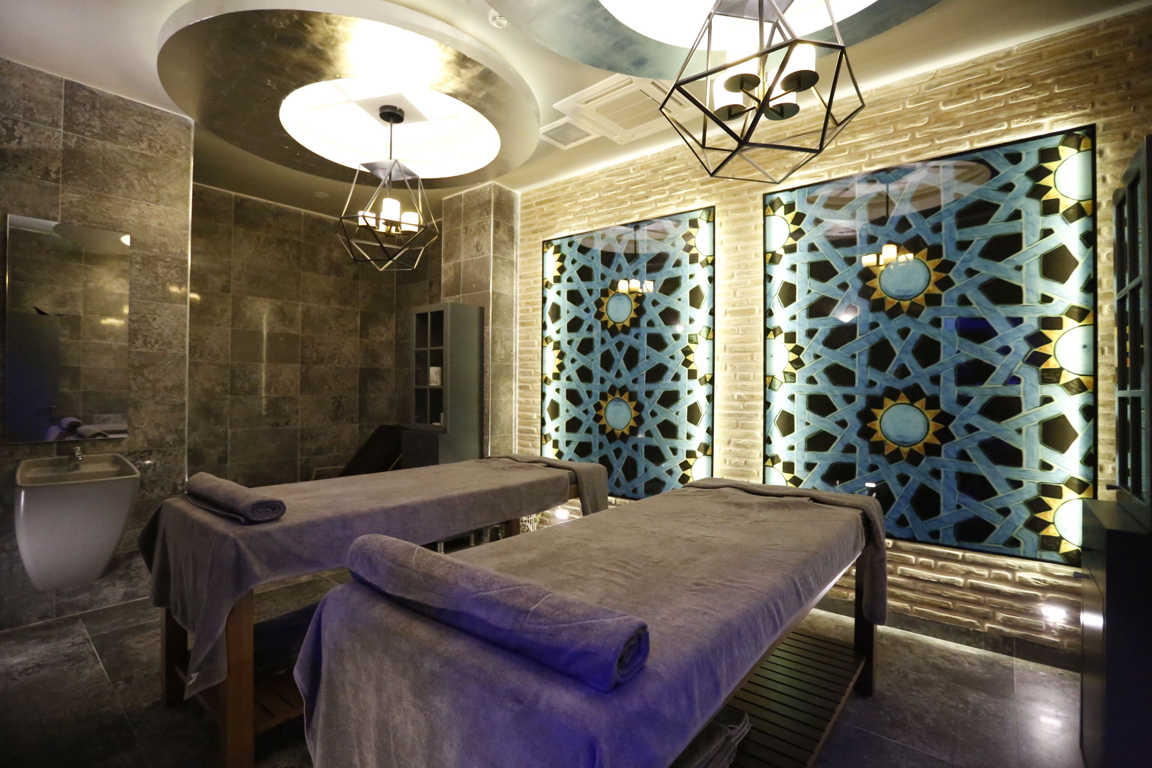 Uma sala de spa com duas mesas de massagem, uma banheira e uma parede decorativa com padrões geométricos.