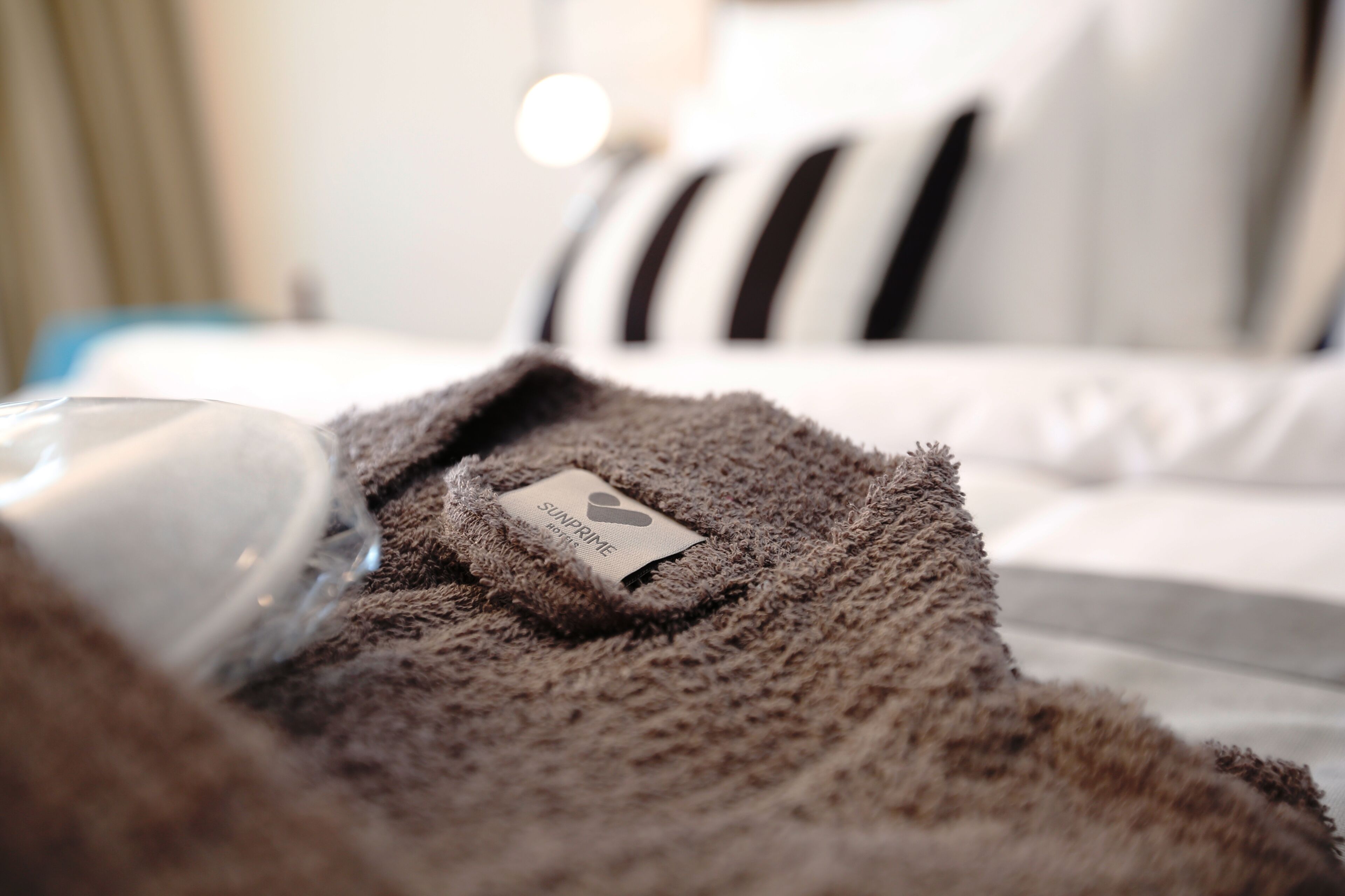 Cama de hotel com uma toalha castanha e uma garrafa em cima.