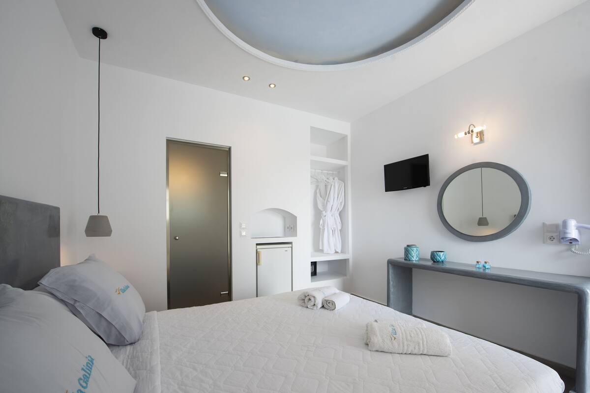 Quarto de hotel moderno com uma cama bem arrumada, um espelho grande, uma televisão e um guarda-roupa.