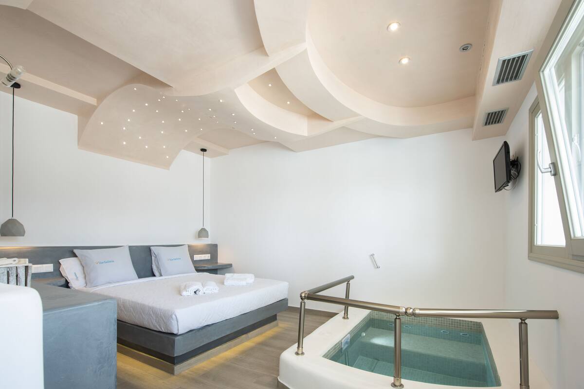 Quarto de hotel moderno com uma cama grande, uma banheira integrada e um design de teto singular.