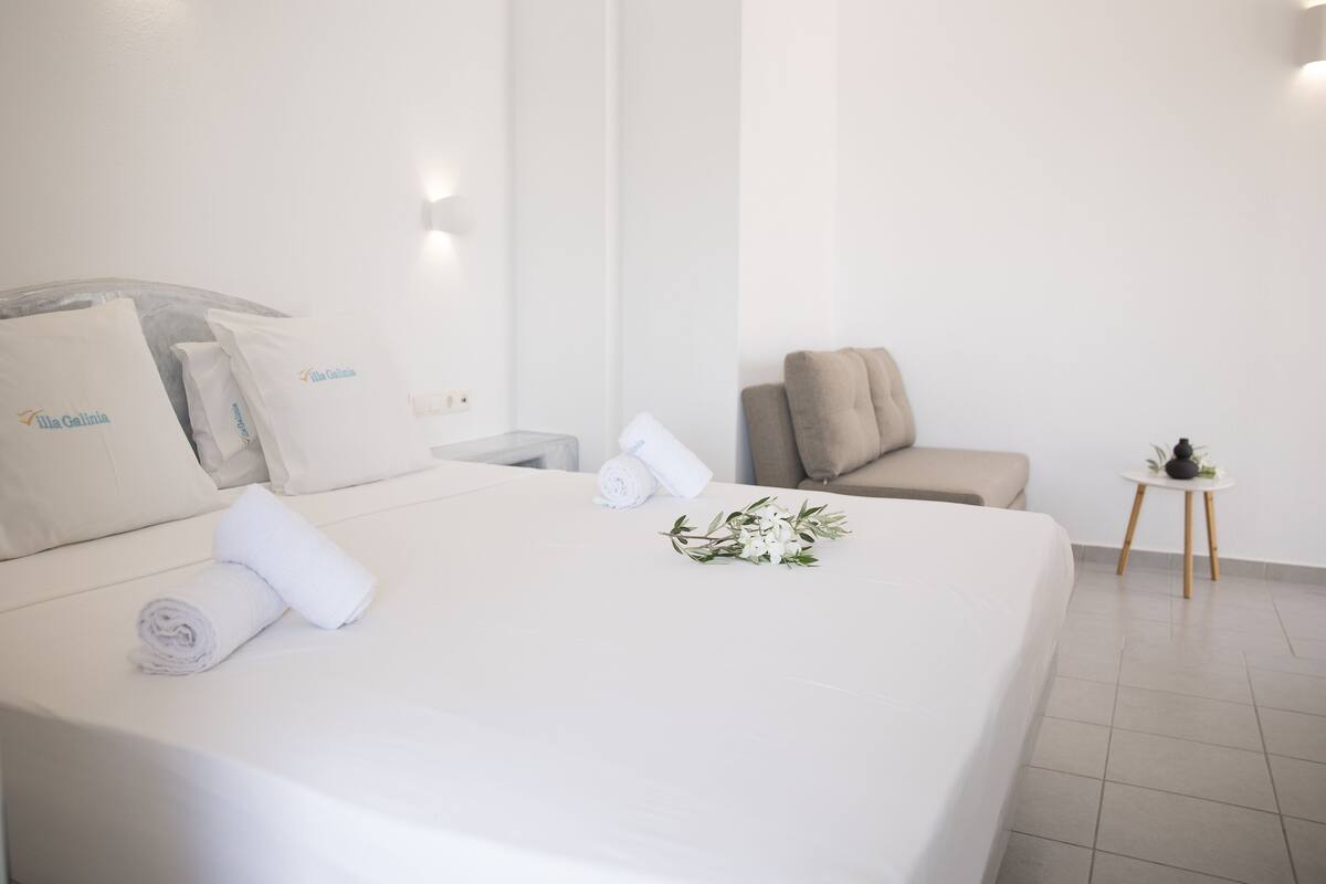 Quarto de hotel com cama bem arrumada, um pequeno espaço de estar e uma mesa de cabeceira com um vaso.