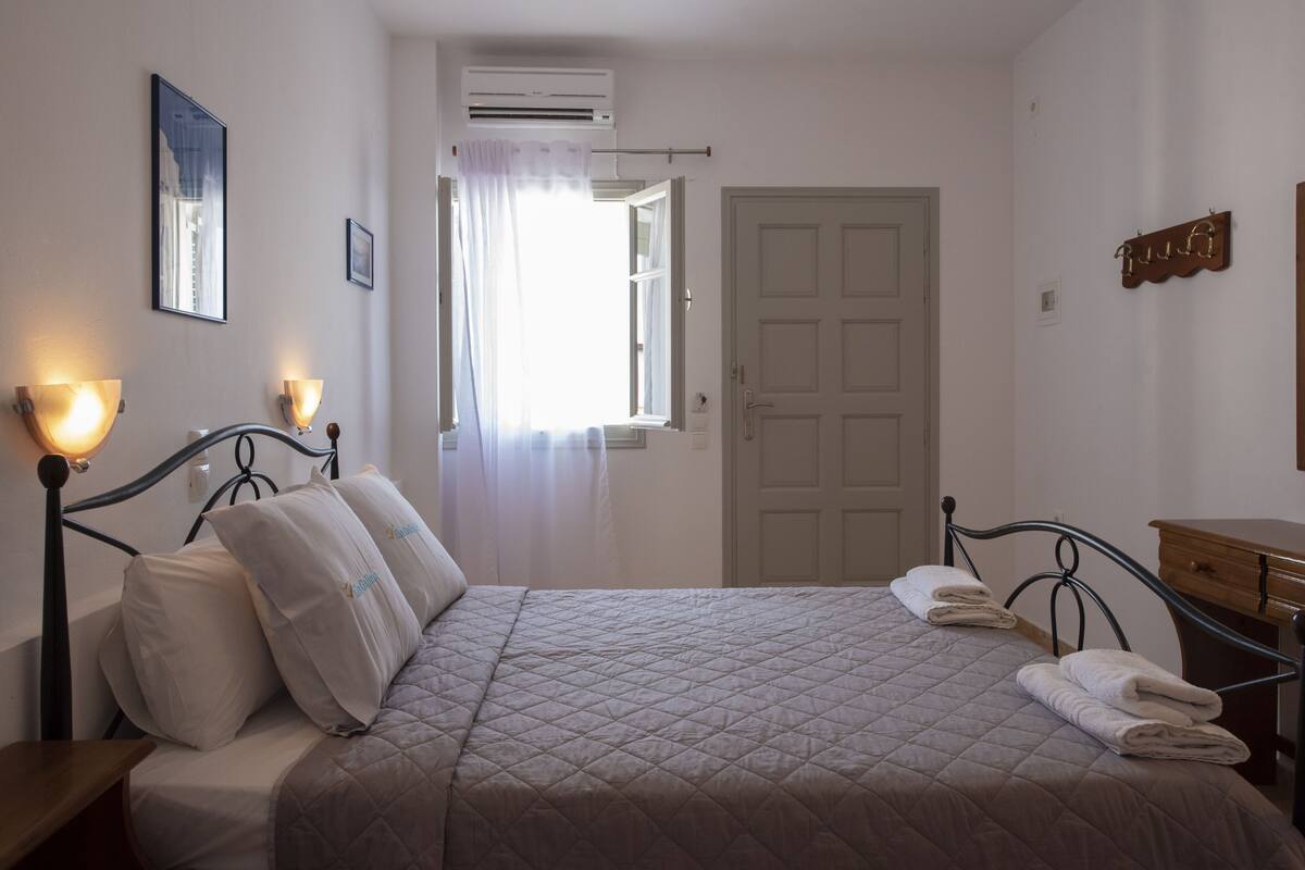 Cama bem arrumada com manta acolchoada, duas luminárias de cabeceira e mesa de cabeceira de madeira.