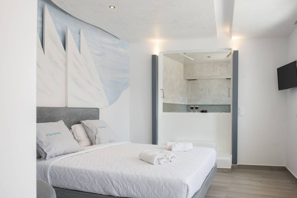 Quarto de hotel moderno com uma cama grande, televisão montada e banheiro com espelho e pia.