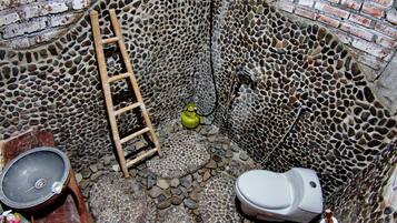 Um banheiro com parede em mosaico de pedra, uma escada de madeira, vaso sanitário e cilindro de gás verde.
