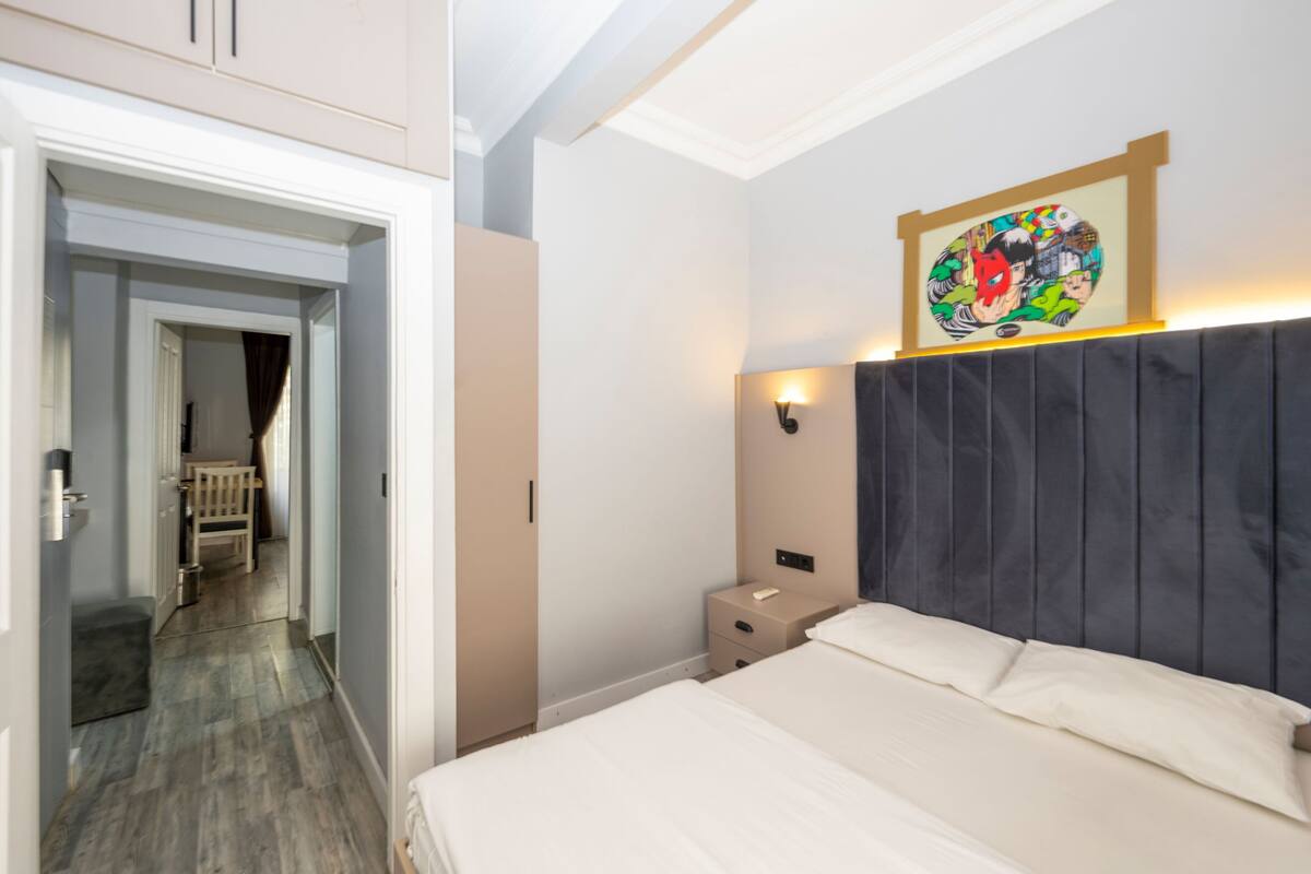 Quarto com cama, mesa de cabeceira e uma obra de arte na parede.