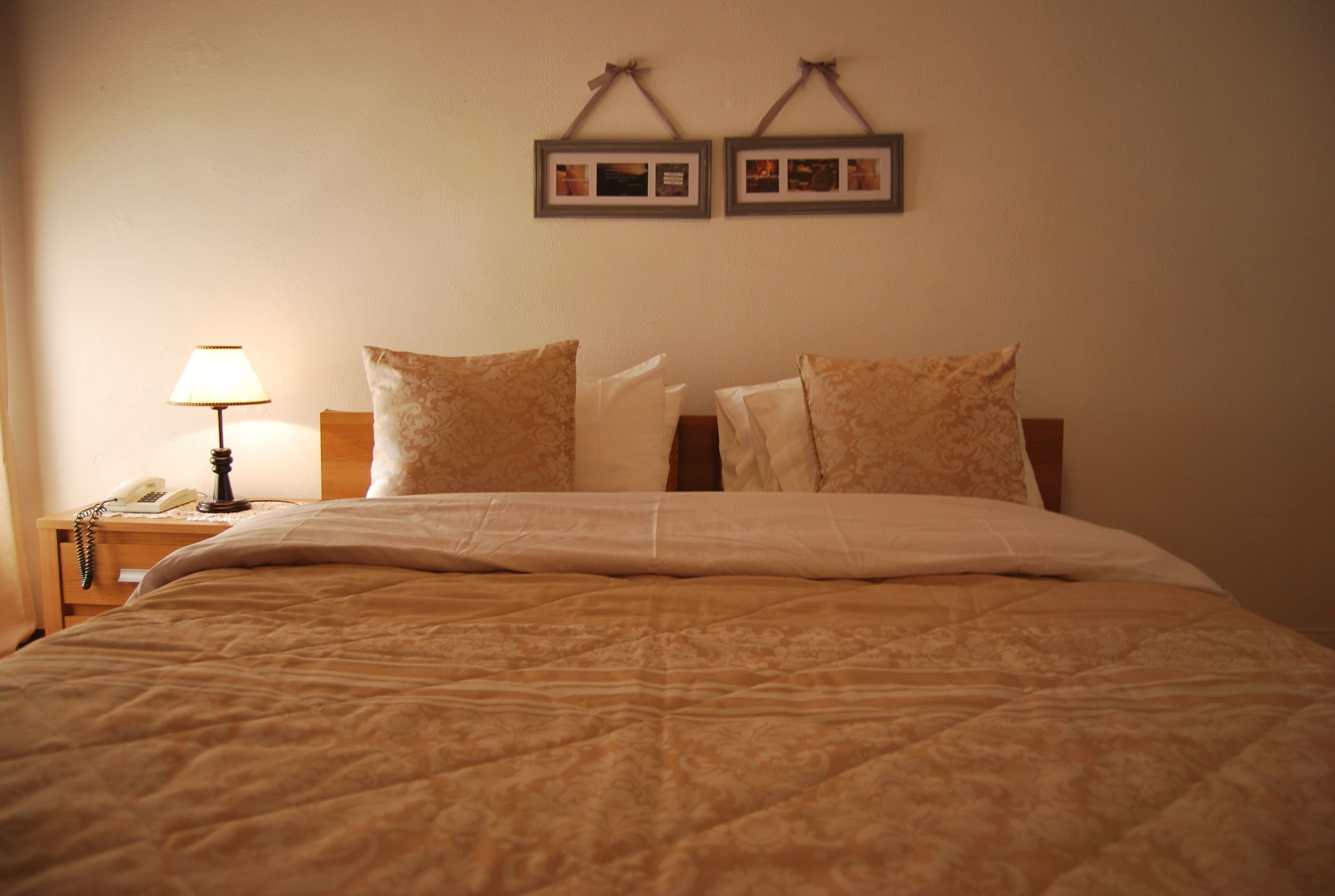 Uma cama bem arrumada com um edredom estampado, duas almofadas, uma luminária de cabeceira e uma mesa de cabeceira com um telefone.