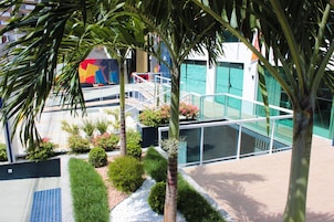 Uma área externa moderna com piscina, palmeiras e um mural colorido em um edifício.