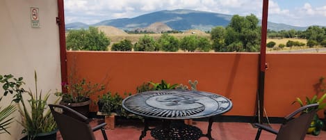 Um pátio com uma mesa redonda e quatro cadeiras, com vista para uma paisagem deslumbrante com montanhas e árvores.