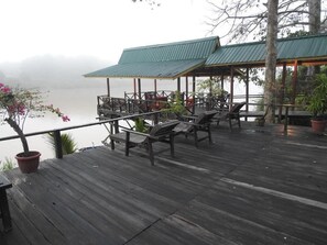 Um deck de madeira com área de estar externa e espaço coberto com vista para a água.
