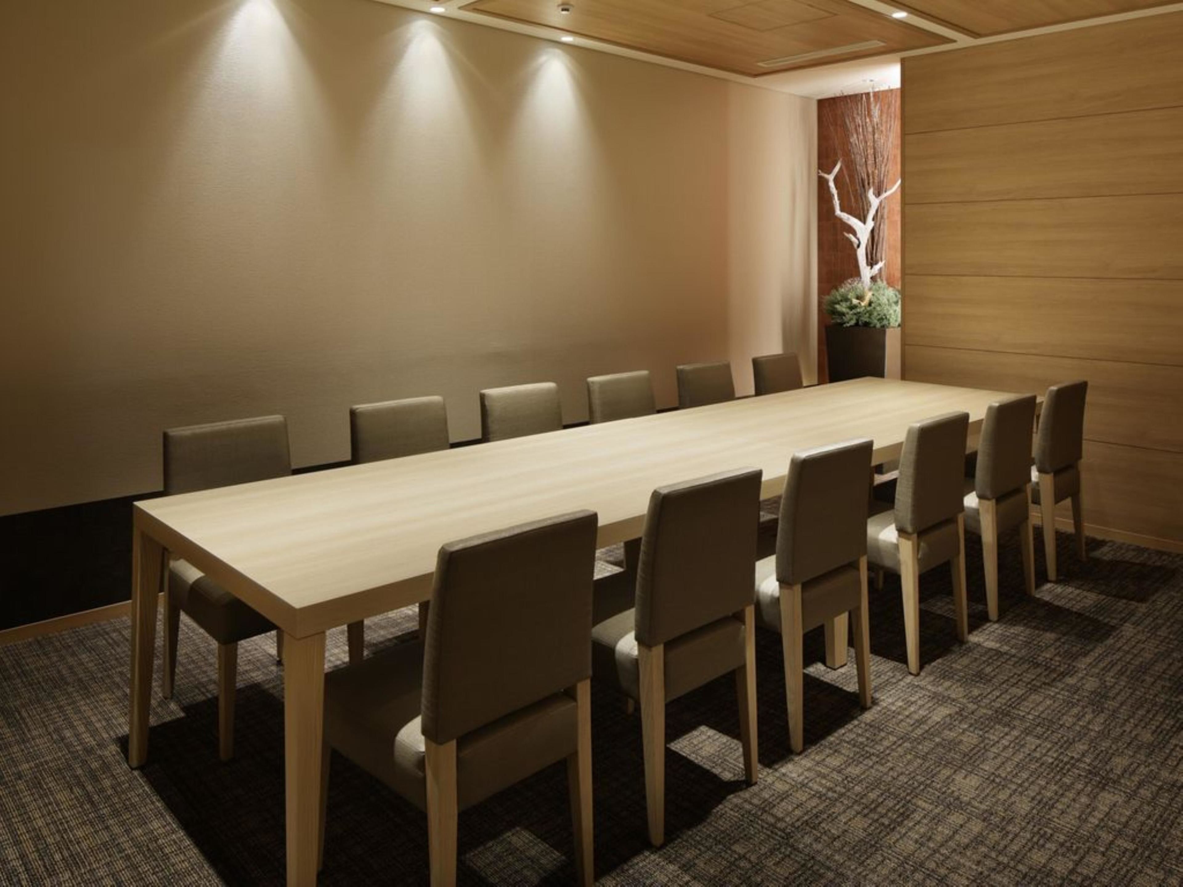 Sala de conferência com uma longa mesa e cadeiras, piso coberto de carpete, paredes revestidas de madeira e iluminação embutida.