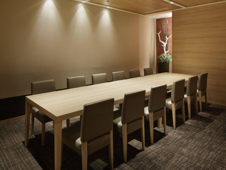 Sala de conferência com uma longa mesa e cadeiras, piso coberto de carpete, paredes revestidas de madeira e iluminação embutida.