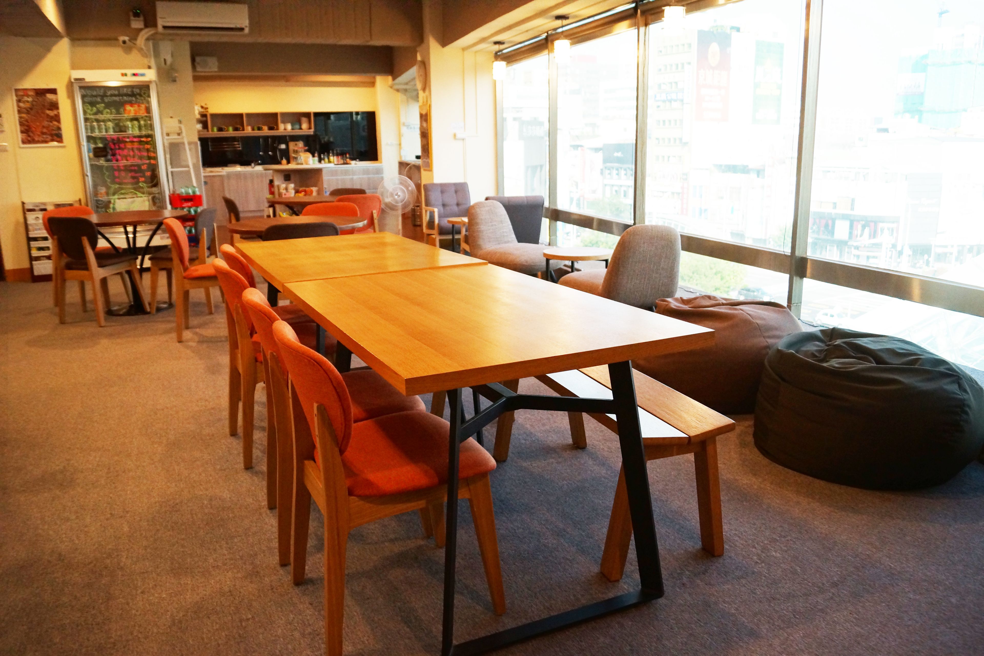 Uma sala de conferências com uma longa mesa de madeira, cadeiras laranja, um puf e vista para a cidade através de grandes janelas.