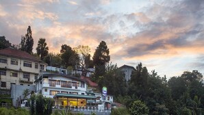 Um hotel com vários andares, uma placa chamativa e vegetação exuberante ao redor.