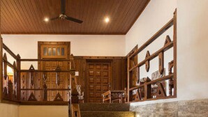 Escada com corrimãos de madeira e ventilador de teto, que leva a um andar inferior com lareira.
