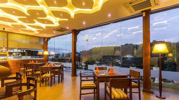 Restaurante com móveis de madeira, grandes janelas e vista para a cidade.