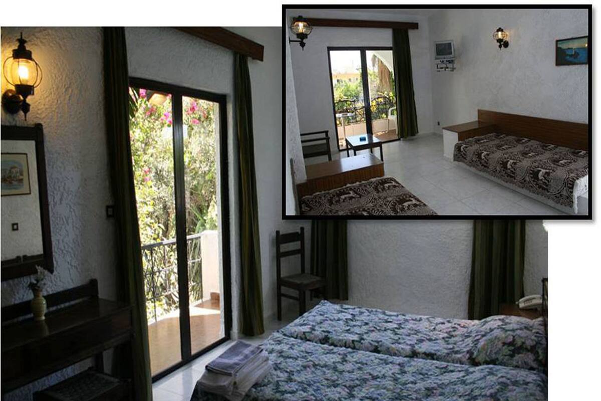 Quarto com cama, escrivaninha e cadeira. Possui varanda vista para vegetação.
