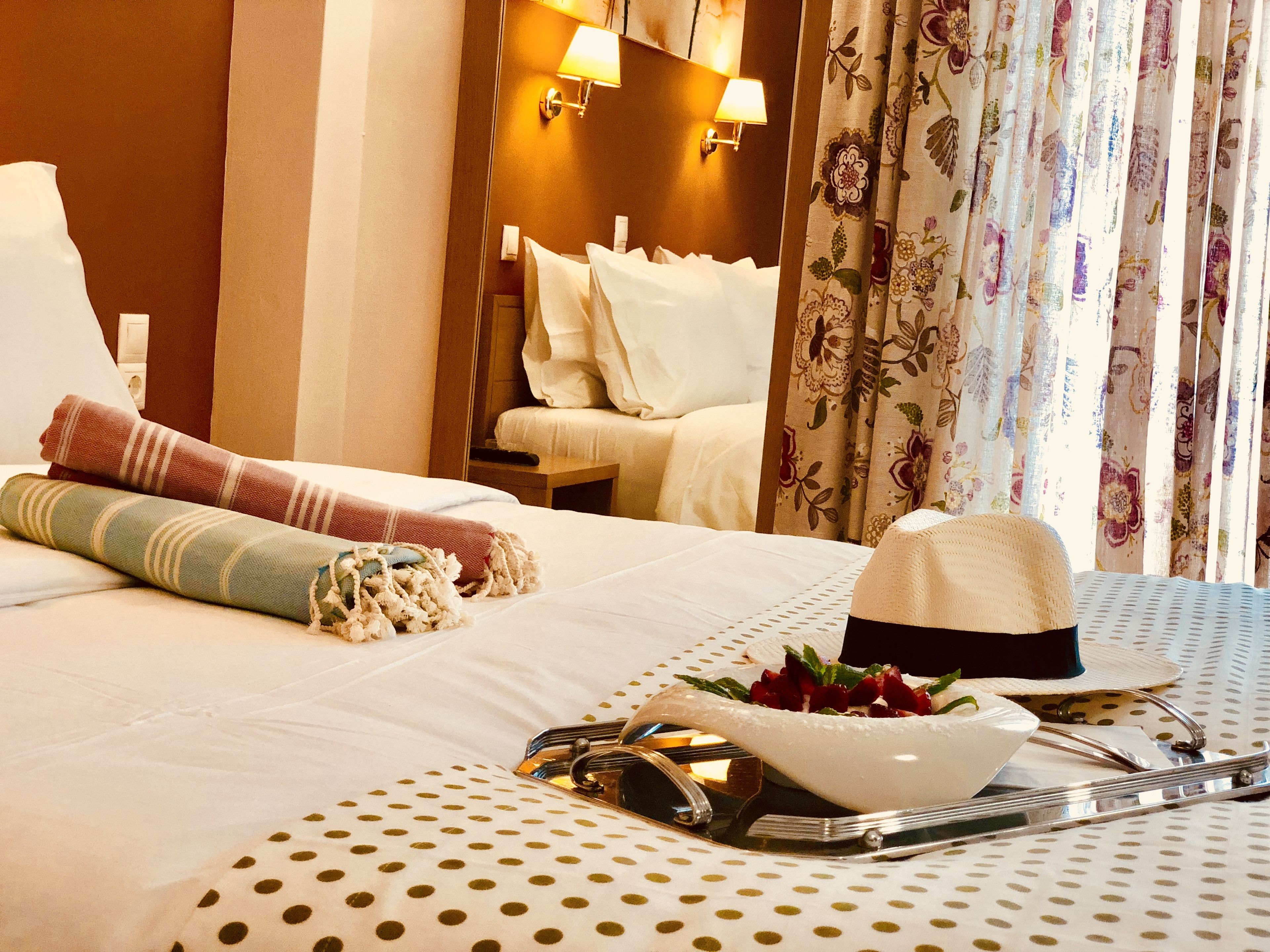 Quarto de hotel com cama bem arrumada, mesa de jantar com talheres e cortina florida.