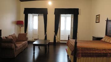 Quarto com sofá, mesa, cama e duas janelas com cortinas.
