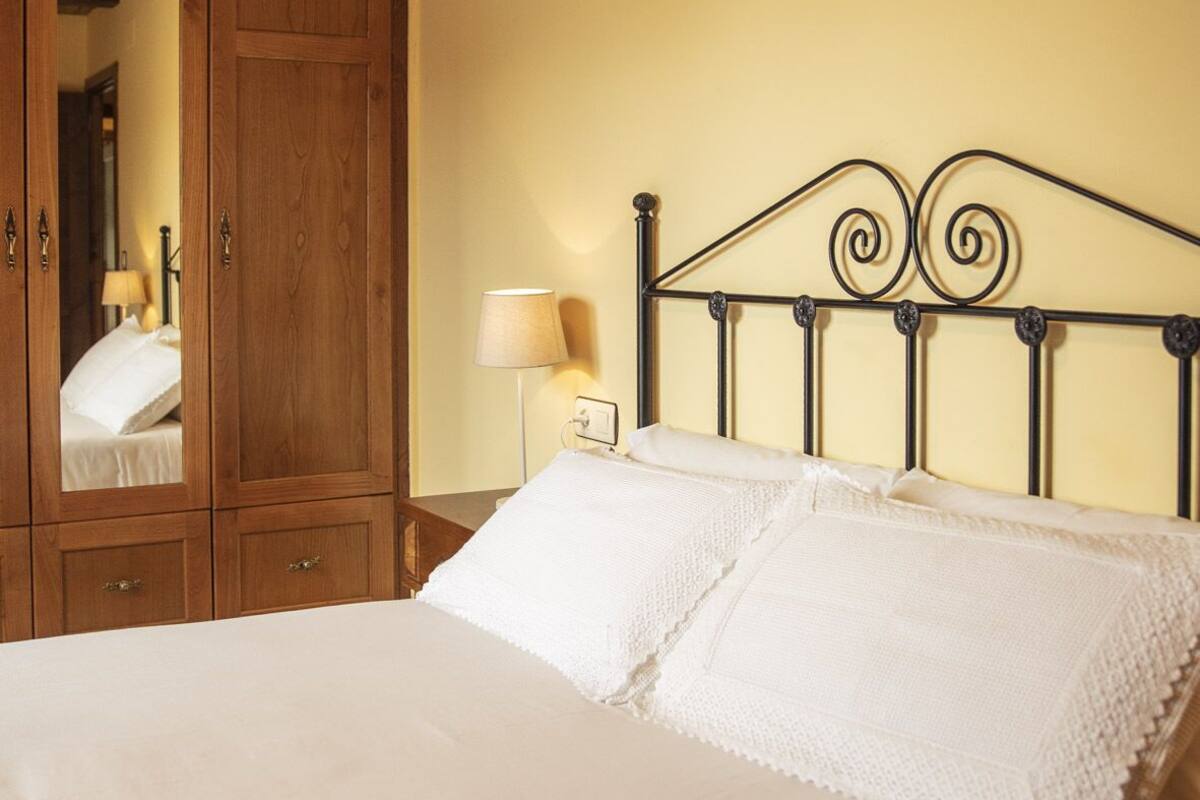 Uma cama bem arrumada com cabeceira de metal, um guarda-roupa de madeira e um abajur.