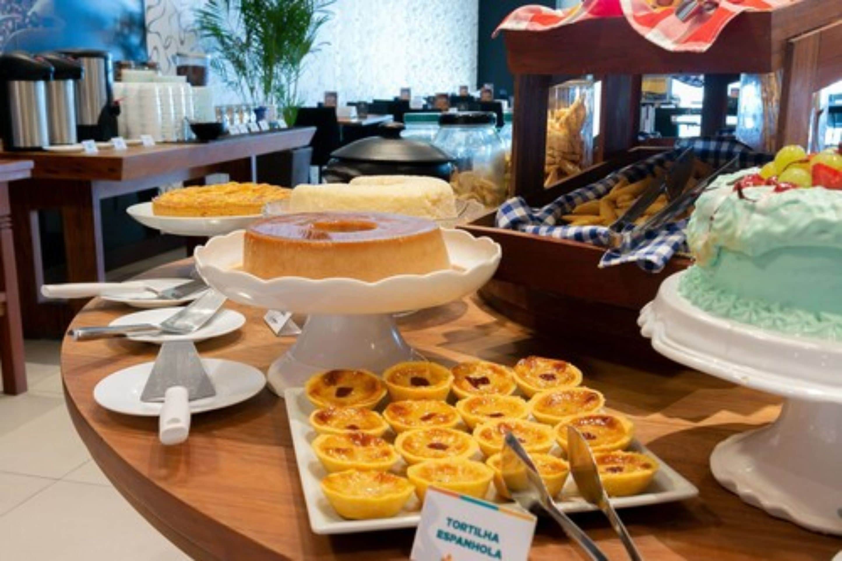 Buffet variado com diversos pratos, incluindo um bolo, doces e uma placa com a indicação 'Tortilla Espanhola'.