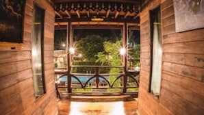 Interior de madeira com varanda e vista para uma piscina e vegetação.