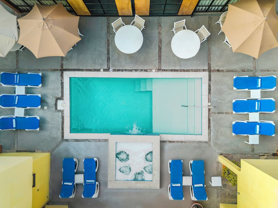 Vista aérea de uma área de piscina com várias espreguiçadeiras, guarda-sóis e uma piscina central.
