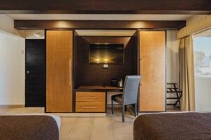 Quarto com cama, escrivaninha com cadeira, televisão e guarda-roupa.