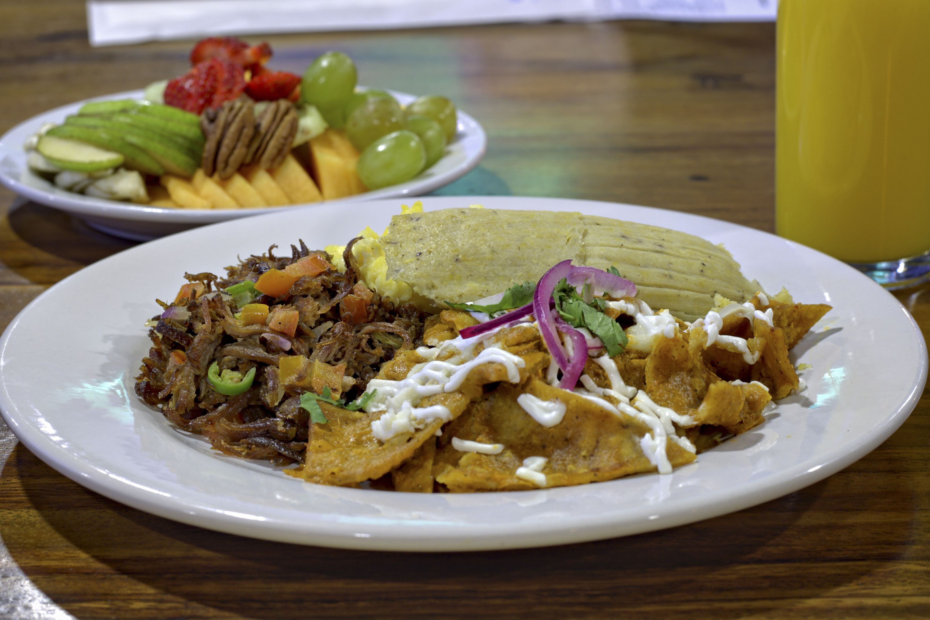 Um prato de nachos com acompanhamentos e uma porção de fruta.