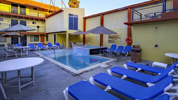 Uma área com piscina, cadeiras de descanso, guarda-sóis e uma piscina pequena.