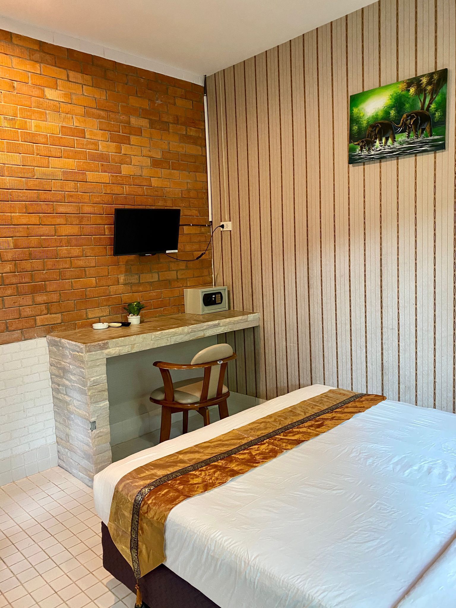 Quarto de hotel com parede de tijolos, uma TV de tela plana acima de uma escrivaninha, uma cadeira e uma cama com colcha estampada.