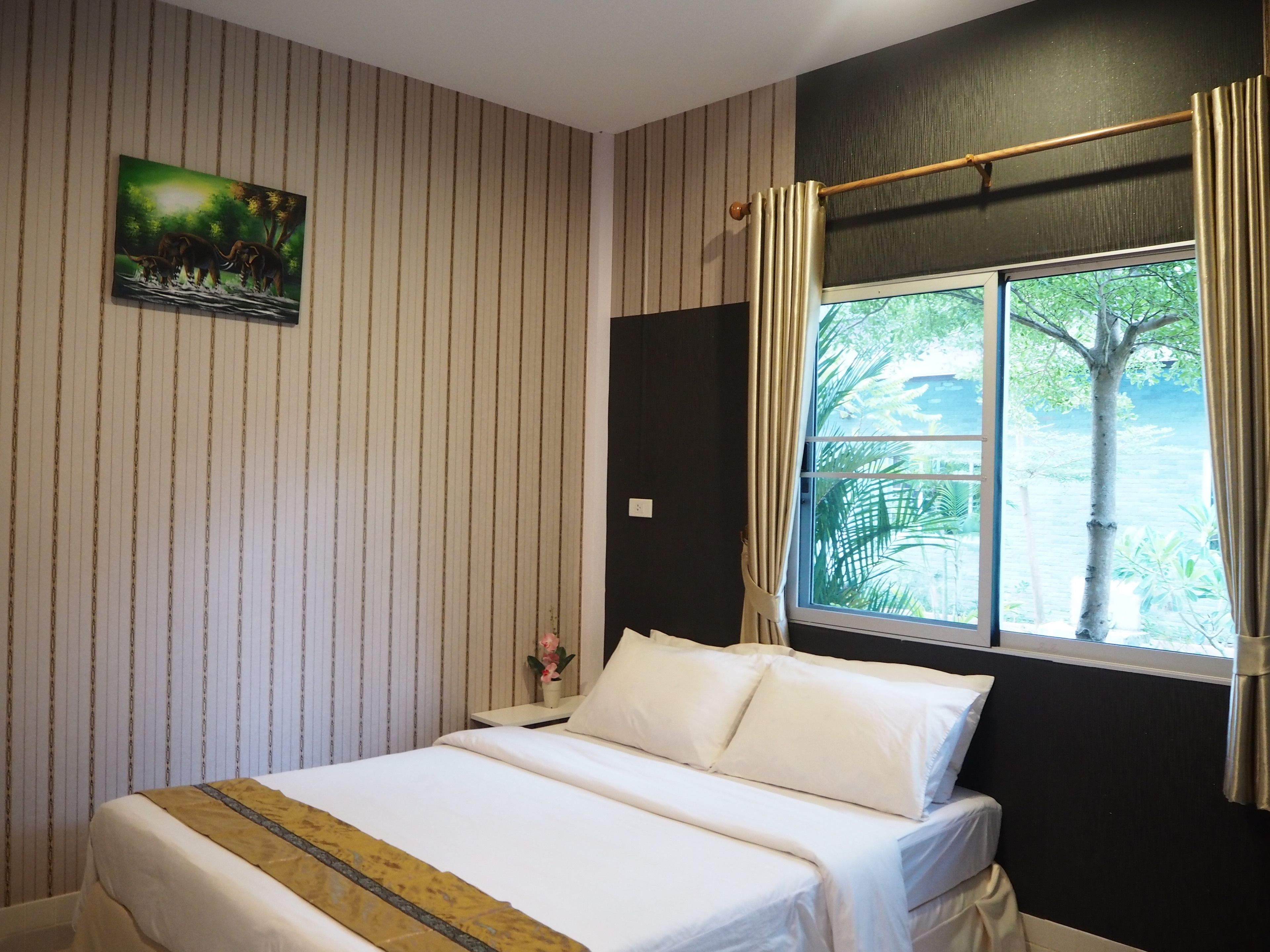 Quarto com cama, janela com cortinas, quadro na parede e mesa de cabeceira com uma flor.