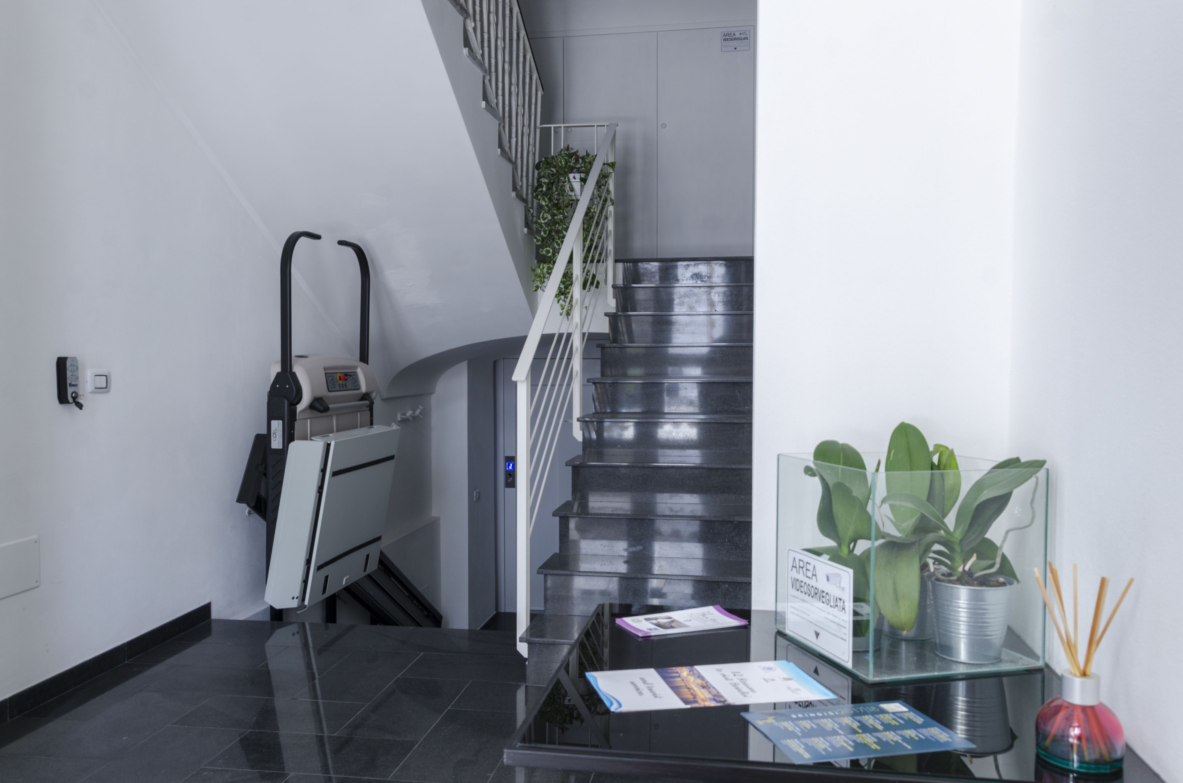 Uma área de recepção com escada, aspirador de pó e uma vitrine de vidro com plantas.