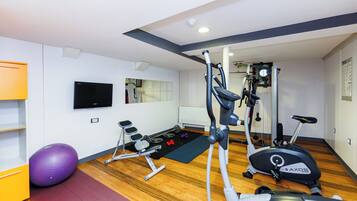 Uma academia com equipamentos de exercícios, uma televisão e um espelho.