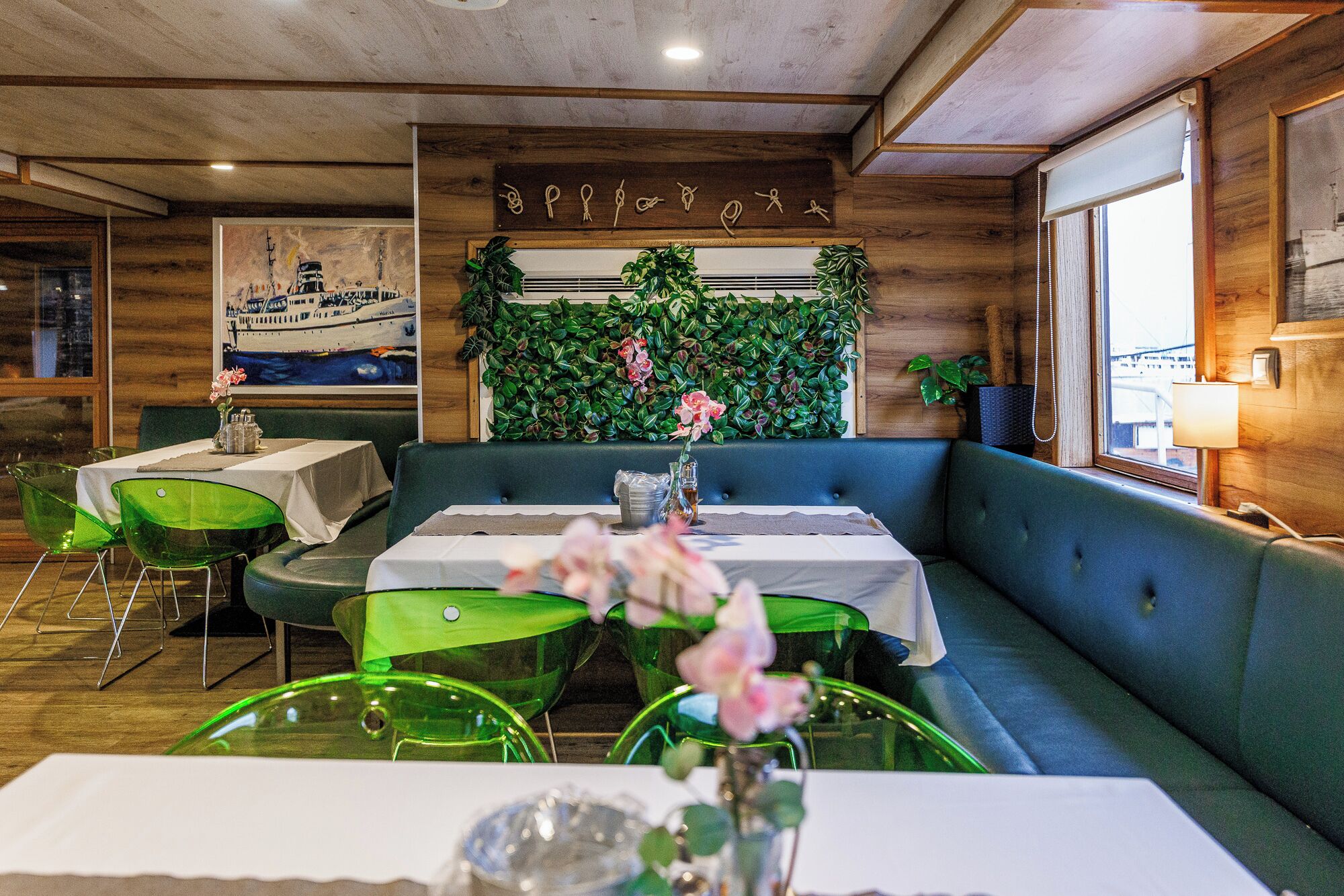 Interior de restaurante com paredes de madeira, assentos estofados em verde e uma janela ampla.