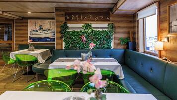 Interior de restaurante com paredes de madeira, assentos estofados em verde e uma janela ampla.
