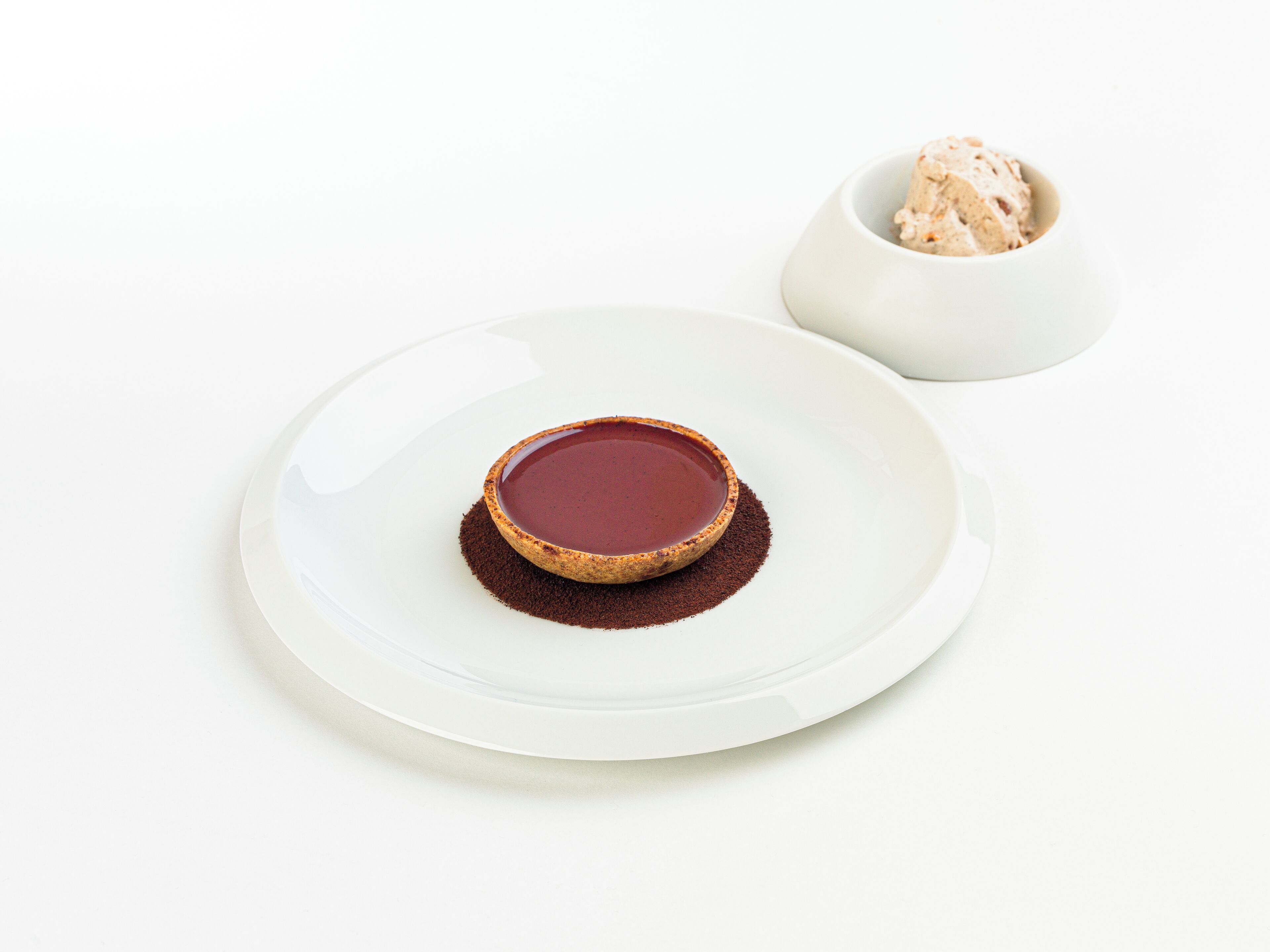 Sobremesa em um prato branco, com uma pequena taça de sorvete ao fundo.