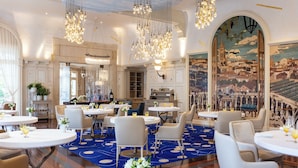 Uma área de refeições luxuosa, com mesas redondas, cadeiras elegantes e um tapete azul estampado.