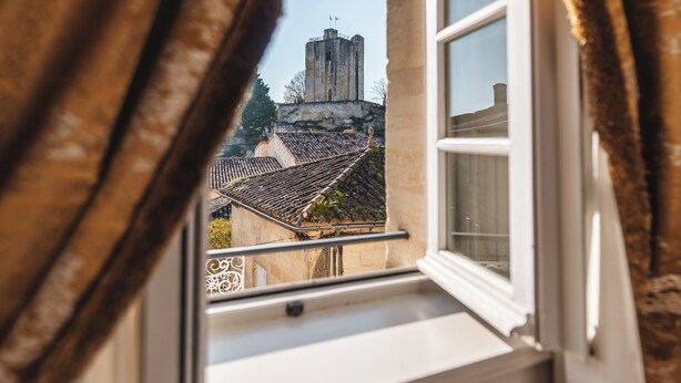 Janela com cortinas, vista de um edifício com torre e céu claro.