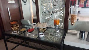 Mesa de buffet de café da manhã com diversos alimentos e um dispensador de suco.