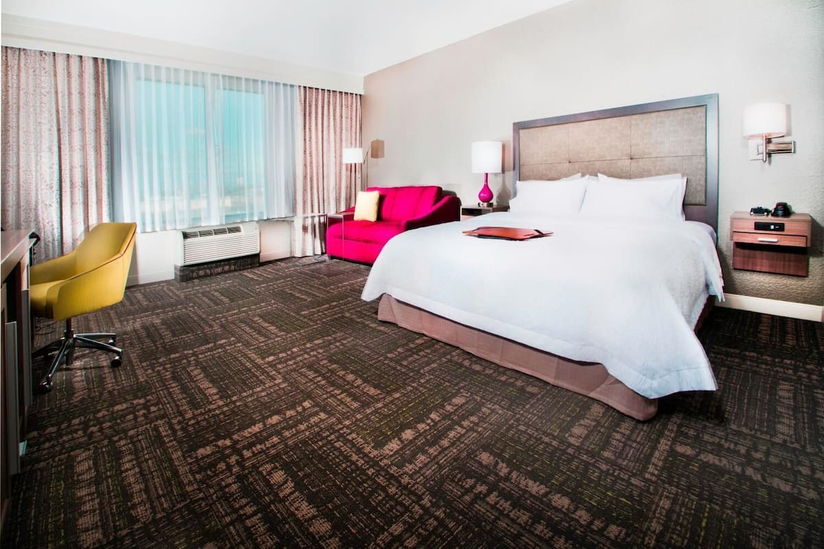 Quarto de hotel com uma cama grande, um sofá vermelho, uma cadeira amarela e uma escrivaninha.