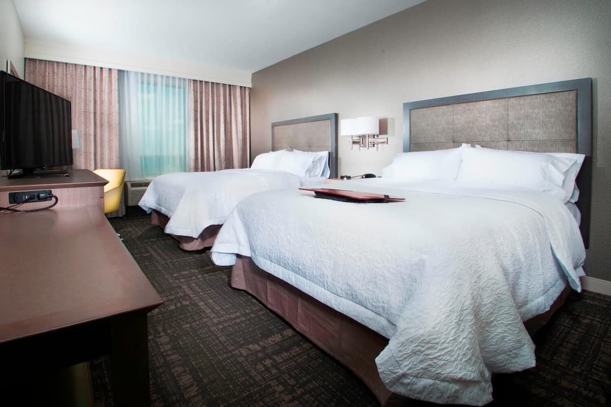 Quarto de hotel com duas camas, uma escrivaninha com televisão e uma cadeira.