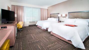Quarto de hotel com duas camas, uma mesa de trabalho com televisão, uma cadeira e janela com cortinas.