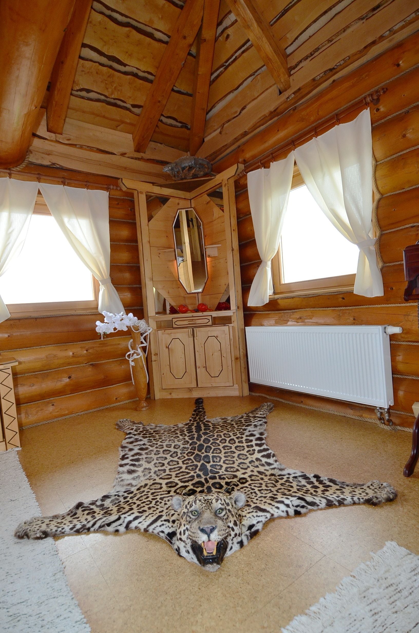 Interior de cabana de madeira com paredes de madeira, tapete de pele de leopardo, espelho e radiador.