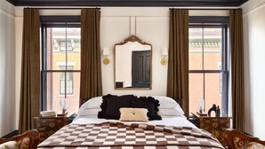 Quarto de hotel com colcha xadrez, um espelho grande sobre a cama e duas janelas com cortinas.