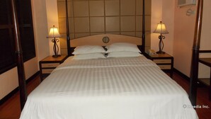 Cama bem arrumada com cabeceira, duas luminárias laterais e ar condicionado fixado na parede.