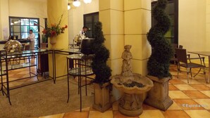 Um saguão de hotel com um balcão de recepção, uma grande fonte decorativa e várias mesas de jantar.